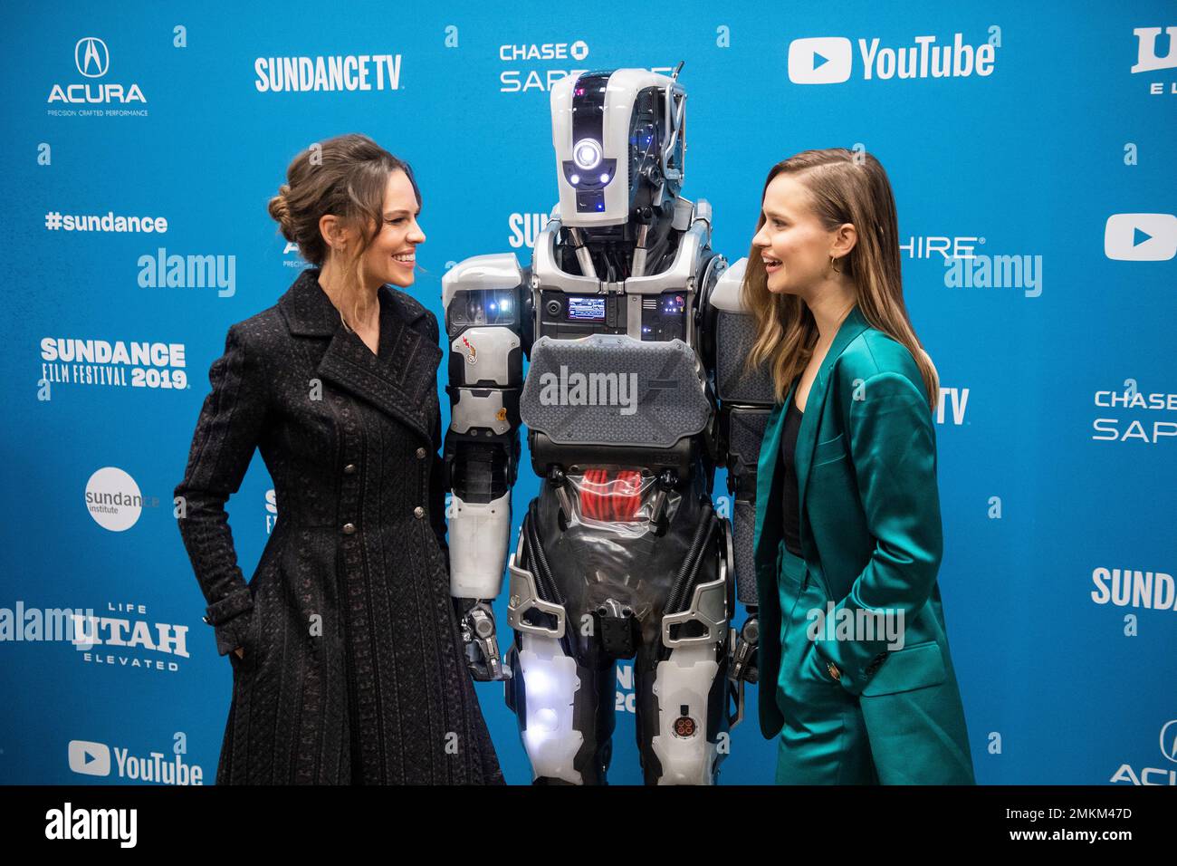 Cast members Hilary Swank, left, and Clara Rugaard pose with a robot ...