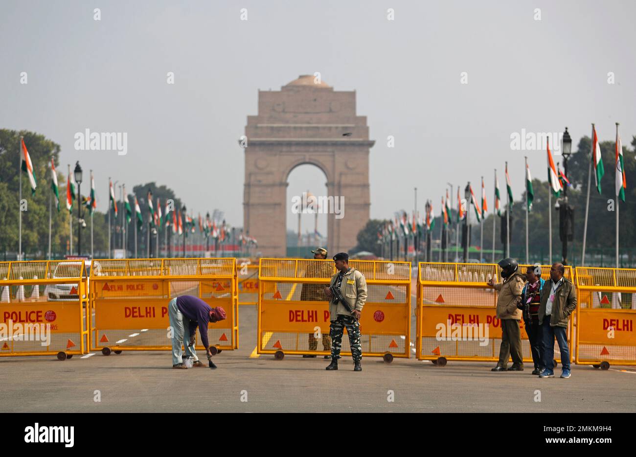 An Indian paramilitary soldier watches a worker paint the road by a ...