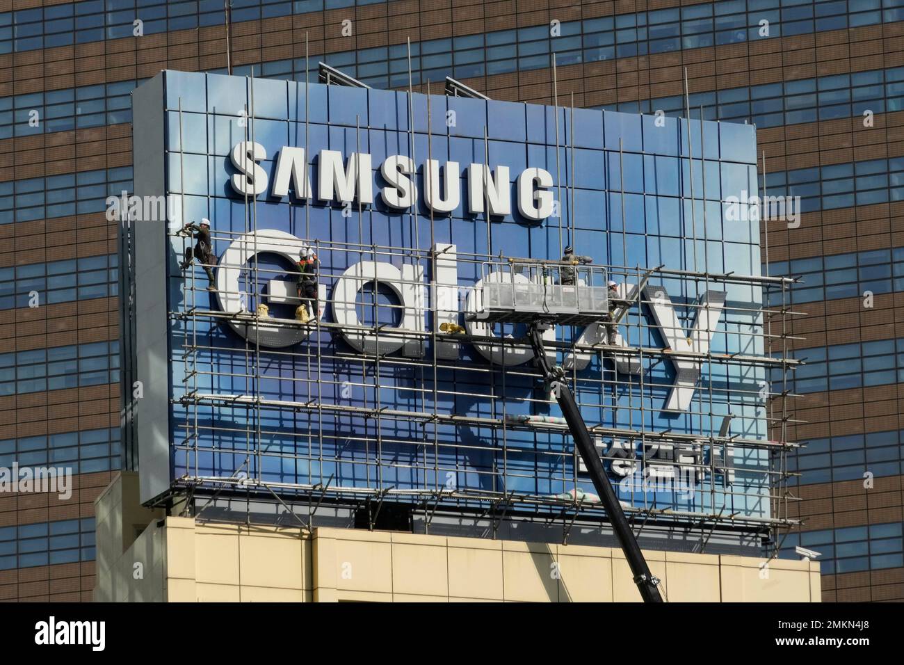 Workers carry materials in front of an advertisement of Samsung ...