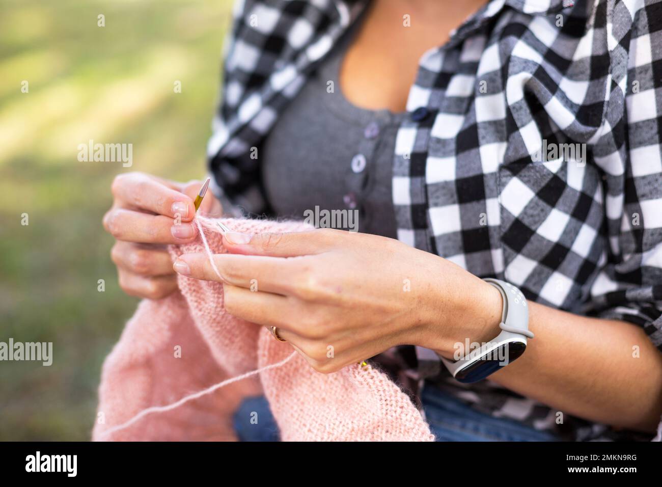 A woman's hands are knitting a woolen cloth from a ball of pink threads ...
