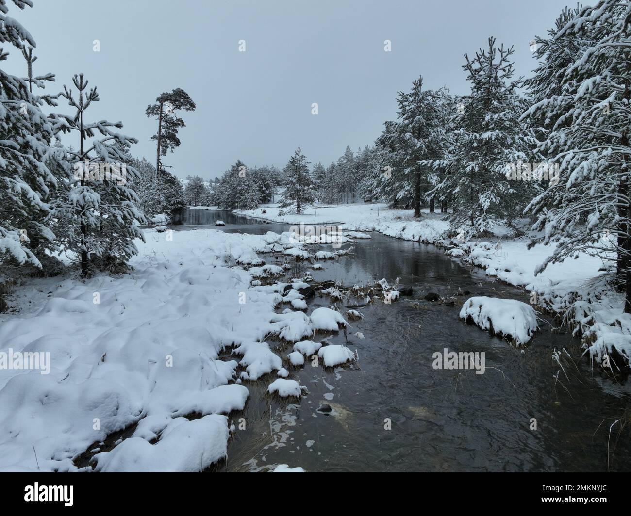 An aerial view of a frozen river flowing through snow-covered forests ...