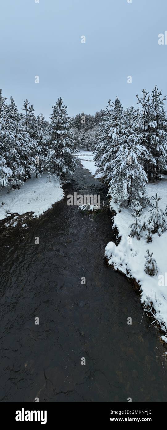 An aerial view of a frozen river flowing through snow-covered forests ...