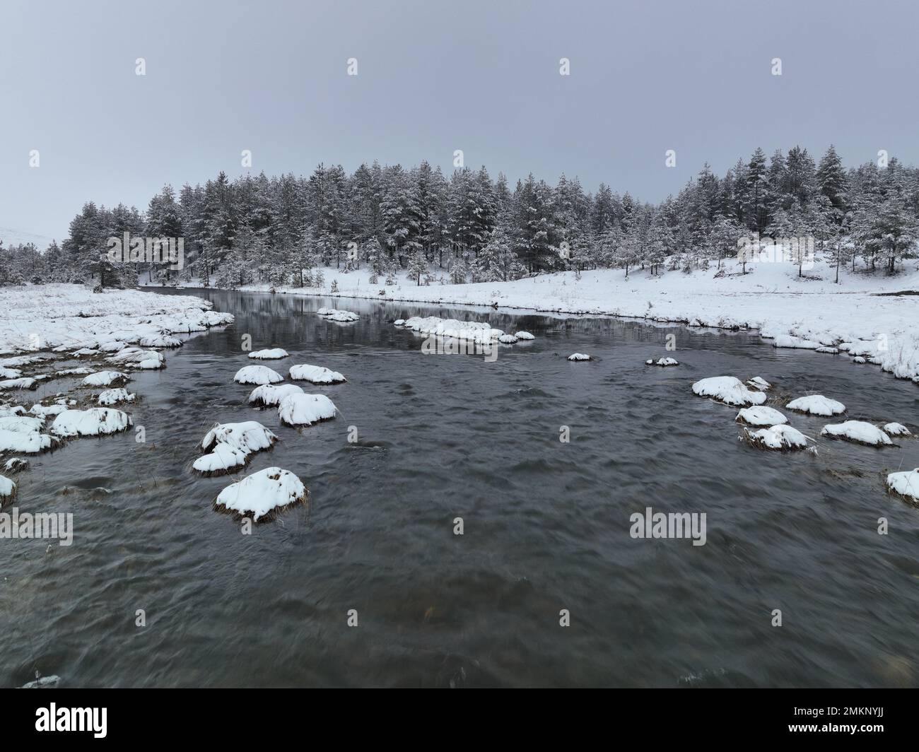 An aerial view of a frozen river flowing through snow-covered forests ...