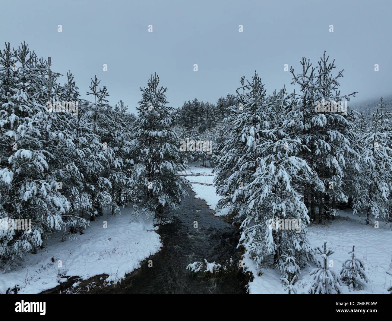 An aerial view of a frozen river flowing through snow-covered forests ...