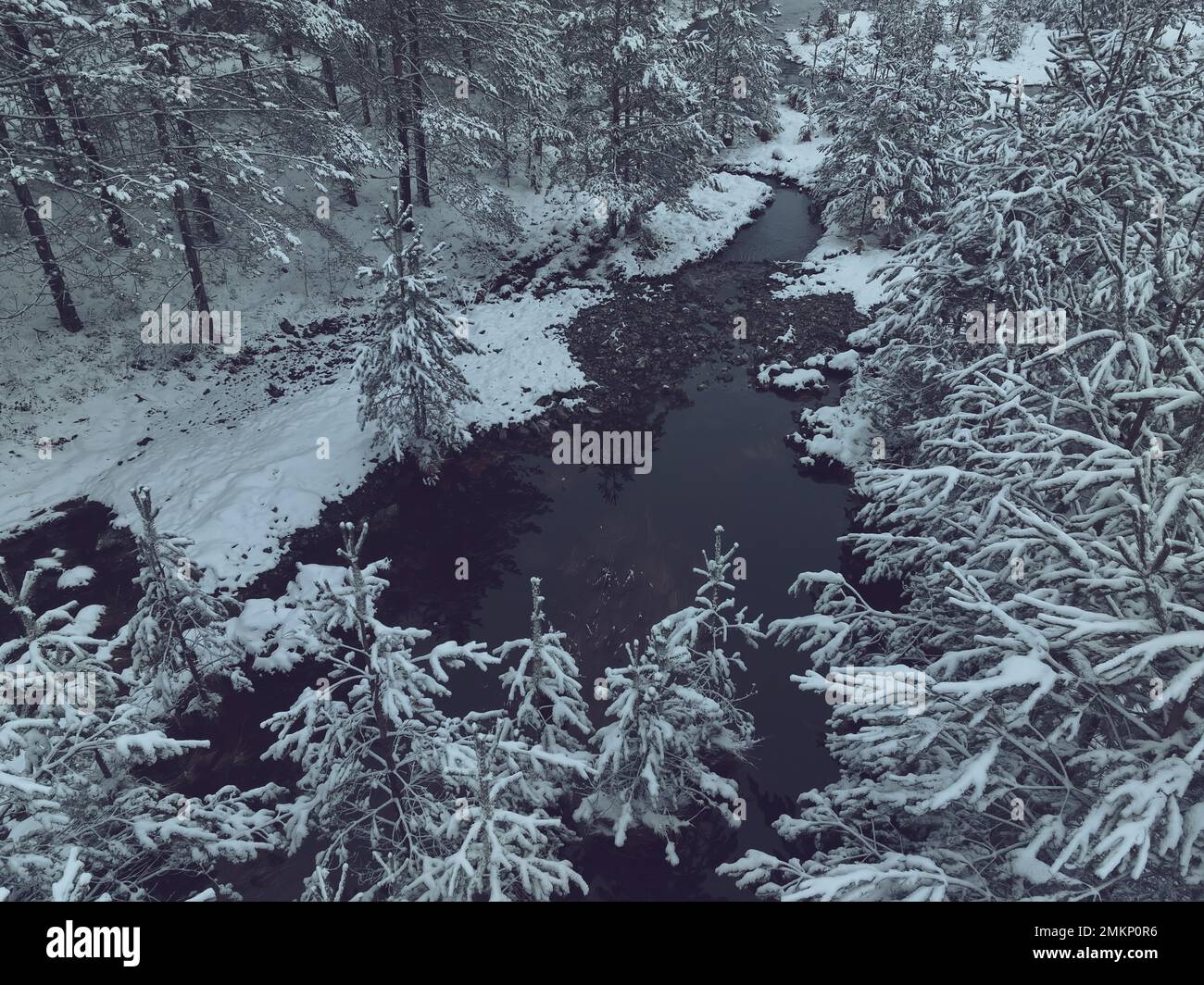 An aerial view of a frozen river flowing through snow-covered forests ...