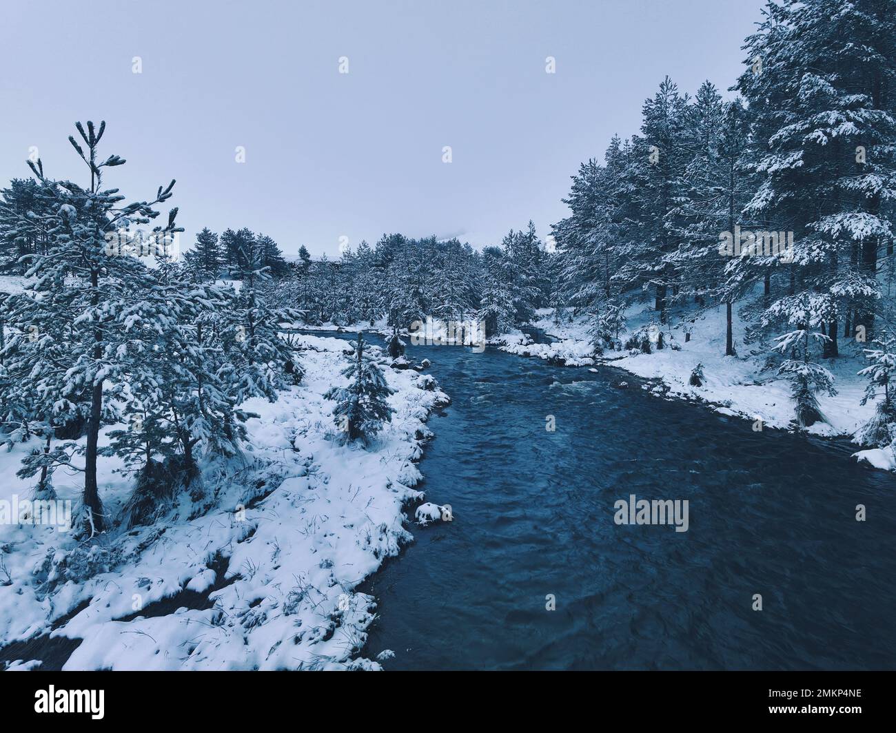 An aerial view of a frozen river flowing through snow-covered forests ...