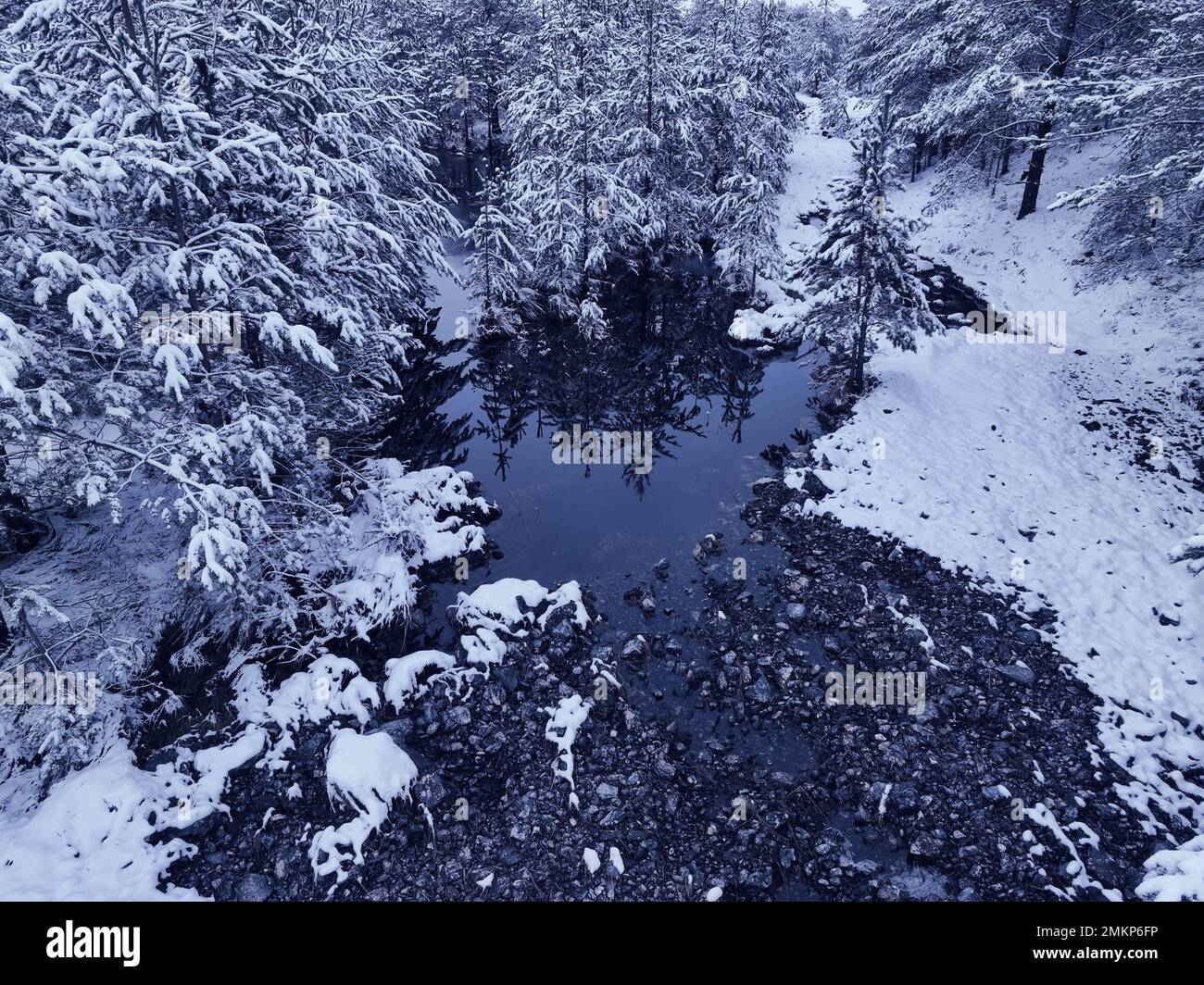 An aerial view of a frozen river flowing through snow-covered forests ...