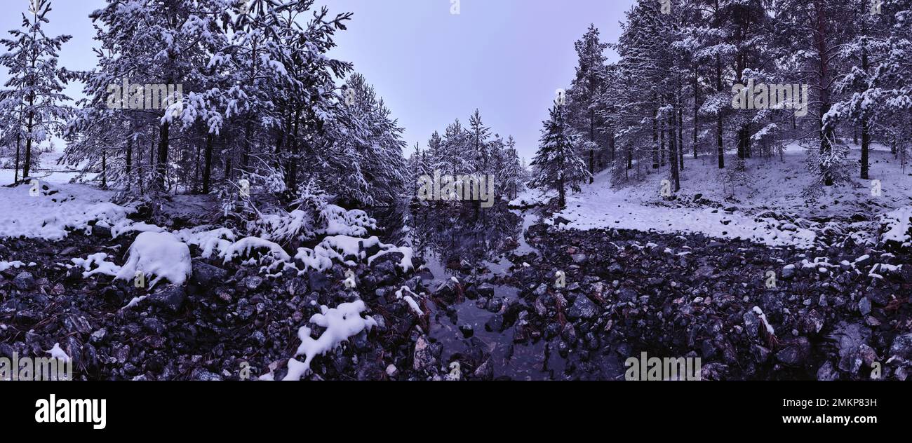 An aerial view of a frozen river flowing through snow-covered forests ...