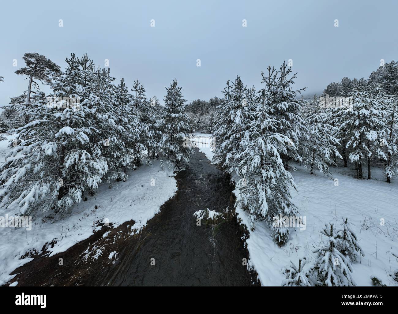 An aerial view of a frozen river flowing through snow-covered forests ...