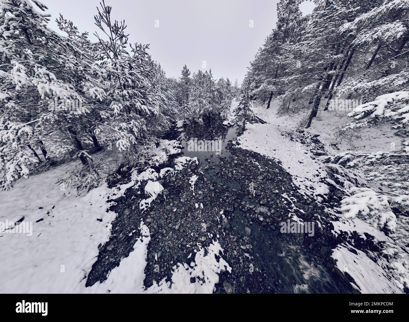 An aerial view of a frozen river flowing through snow-covered forests ...