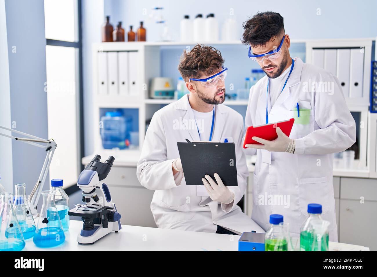 Young couple wearing scientist uniform using touchpad at laboratory ...