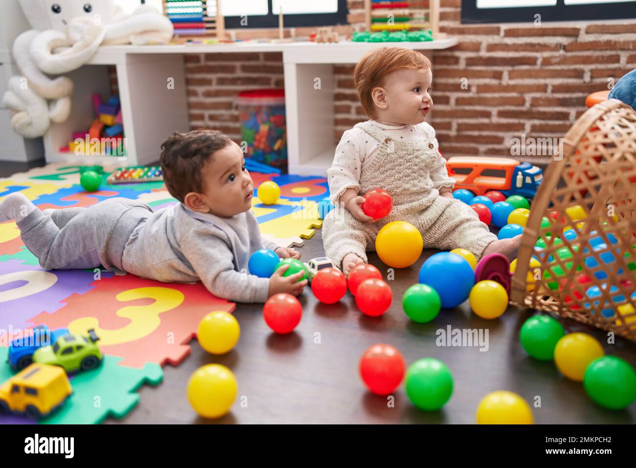 Two adorable babies playing with balls sitting on floor at kindergarten ...