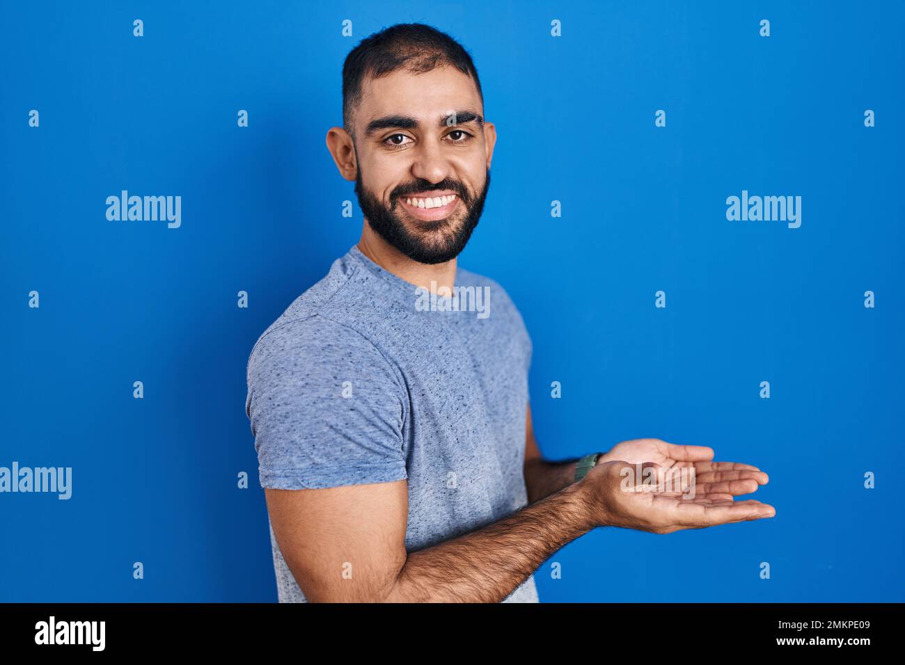 Middle east man with beard standing over blue background pointing aside ...
