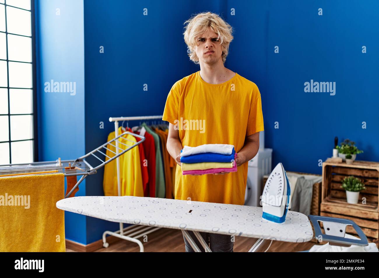 Young man ironing clothes at home depressed and worry for distress ...