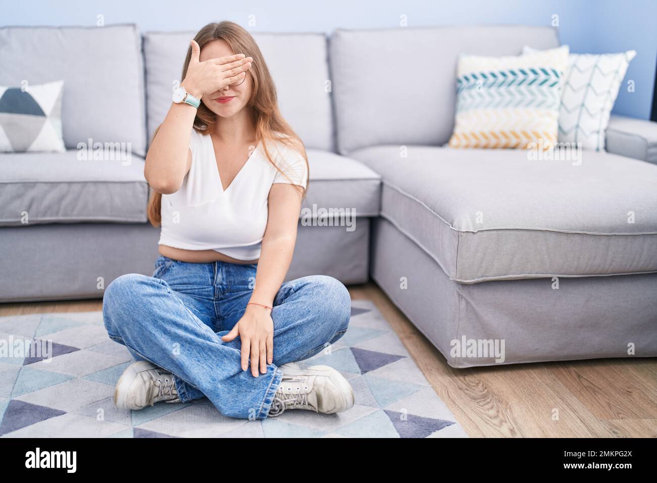 Young caucasian woman sitting on the floor at the living room covering ...