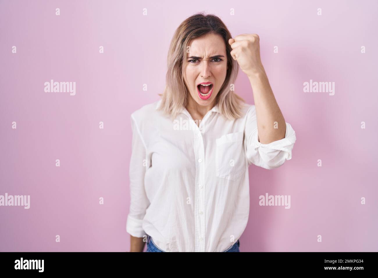 Young beautiful woman standing over pink background angry and mad ...