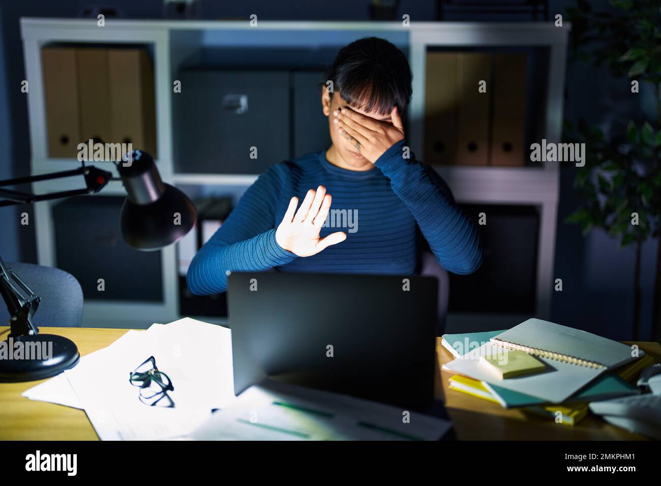 Young beautiful woman working at the office at night covering eyes with ...