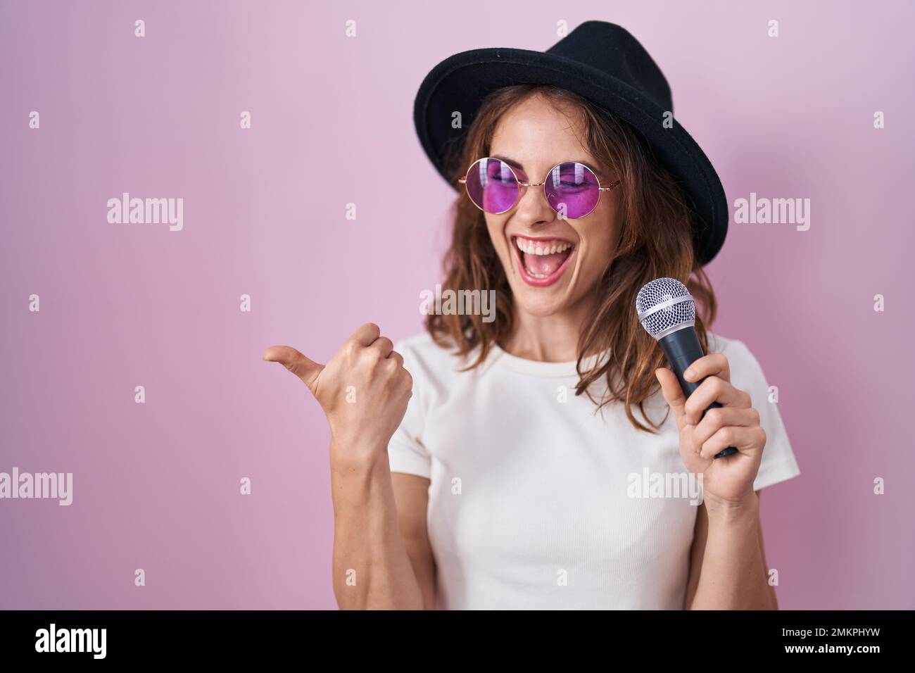 Beautiful brunette woman singing song using microphone pointing thumb ...