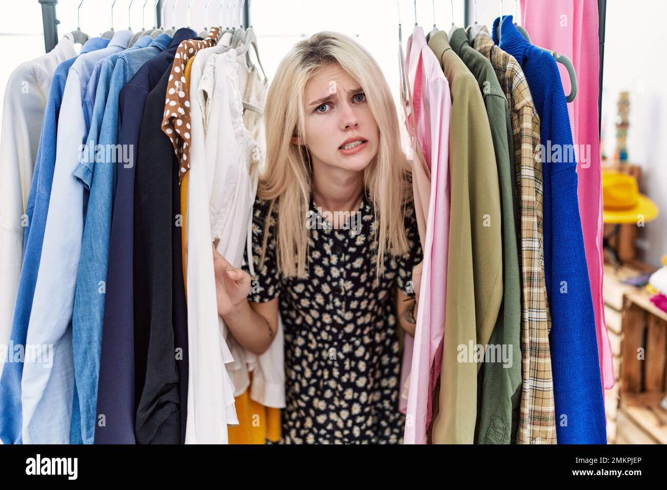 Young blonde woman searching clothes on clothing rack clueless and ...
