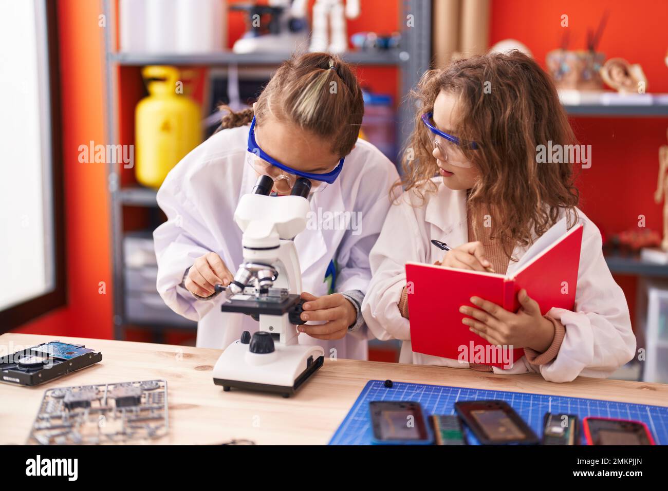 Two kids students using microscope writing on notebook at laboratory ...
