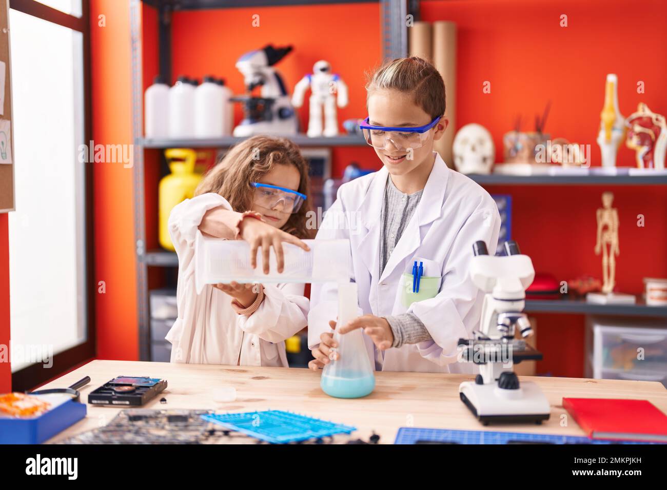Two kids students pouring liquid on test tube at laboratory classroom ...