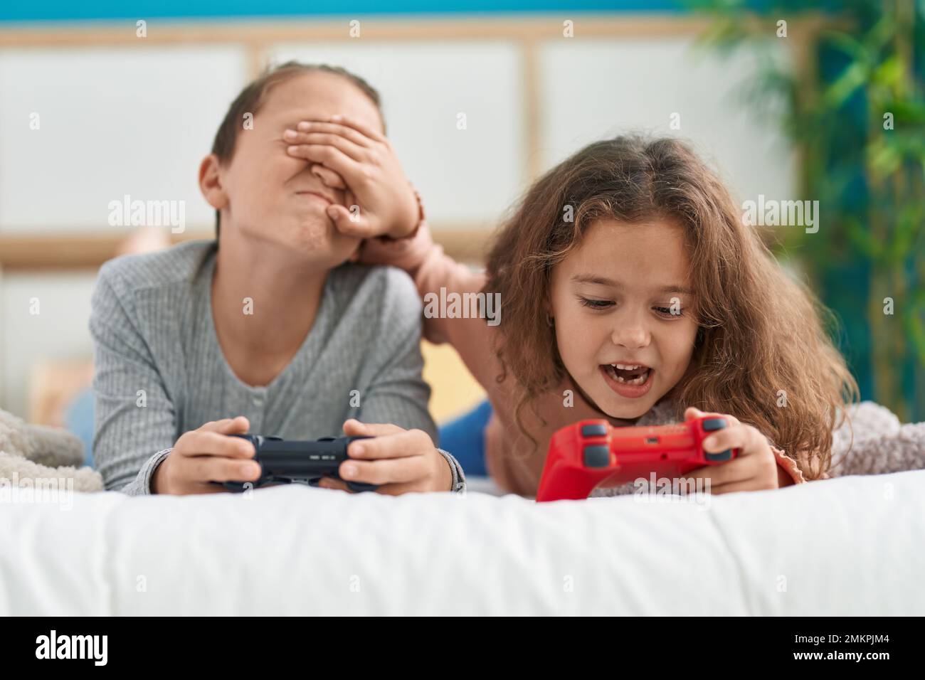 Two kids playing video game lying on bed cheating at bedroom Stock ...
