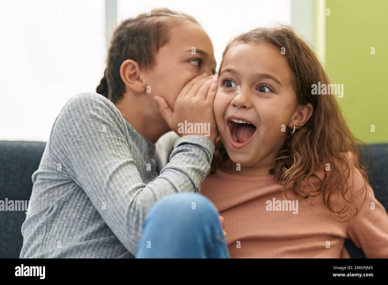 Two kids telling secret sitting on sofa at home Stock Photo - Alamy