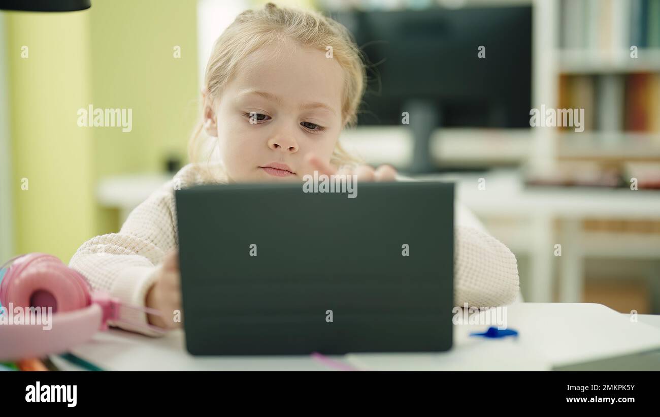Adorable blonde girl student using touchpad sitting on table at ... Adorable blonde girl student using touchpad sitting on table at ...