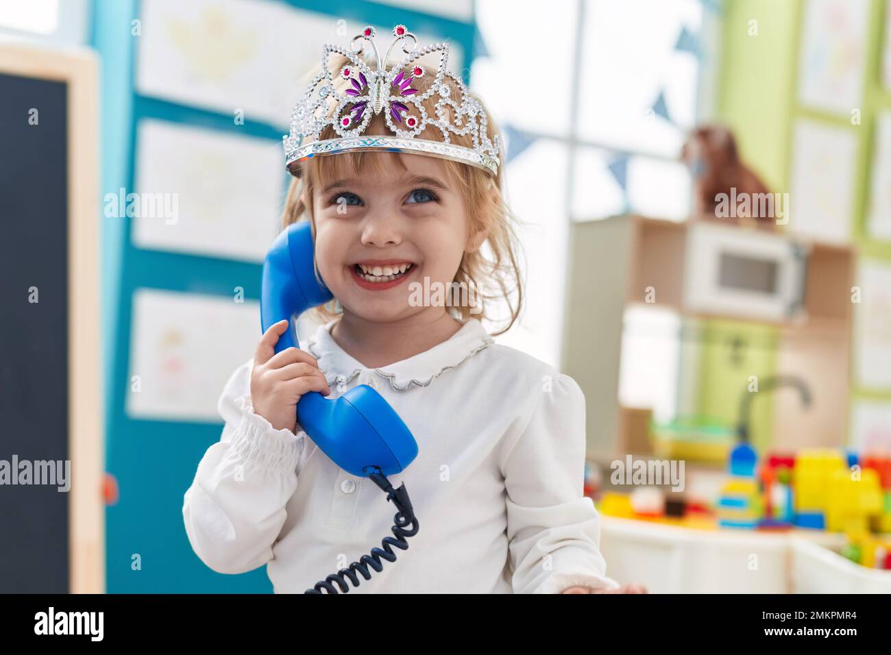Adorable blonde girl wearing princess crown playing with telephone toy ...