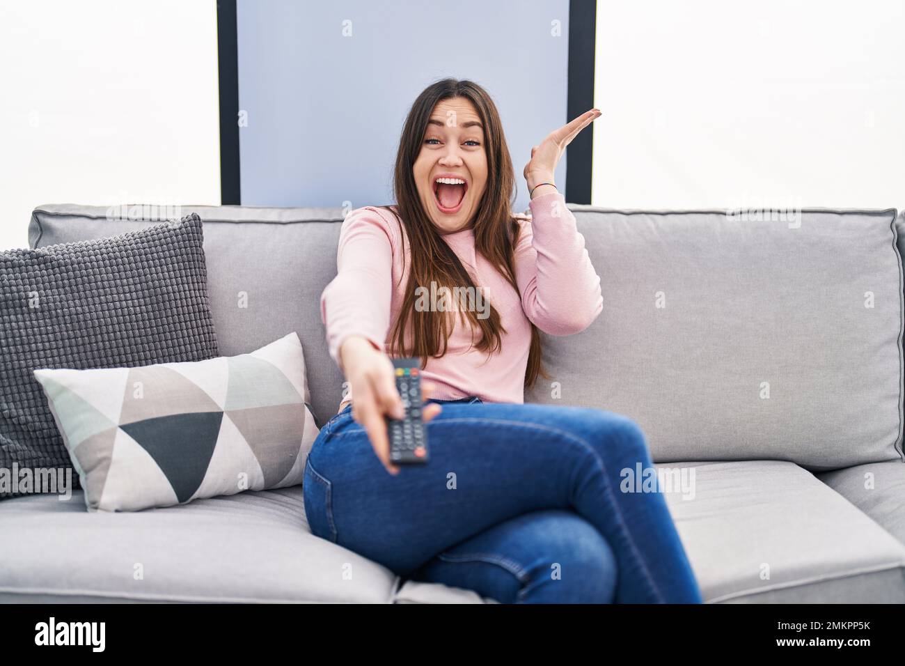 Young brunette woman holding television remote control celebrating ...