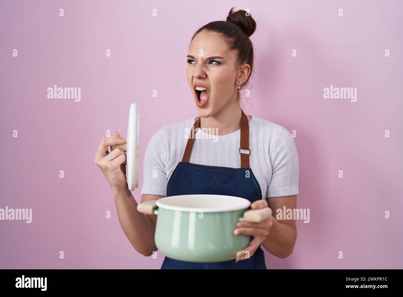 Young hispanic girl wearing apron holding cooking pot angry and mad ...