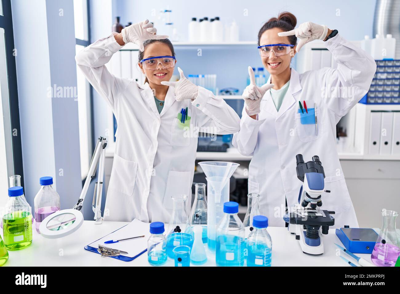Young mother and daughter at scientist laboratory smiling making frame ...
