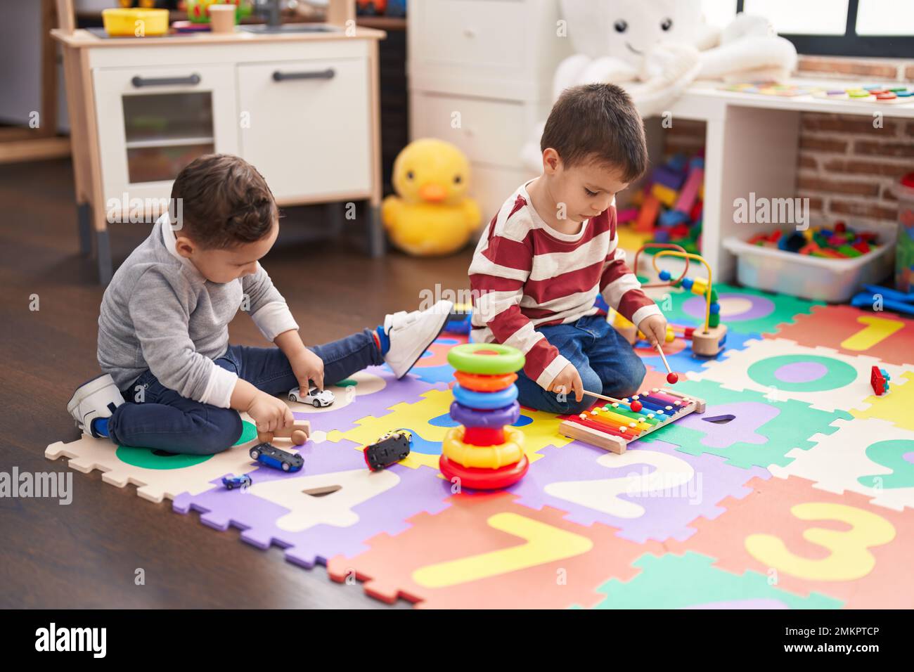 Two kids playing xylophone holding car toy sitting on floor at ...