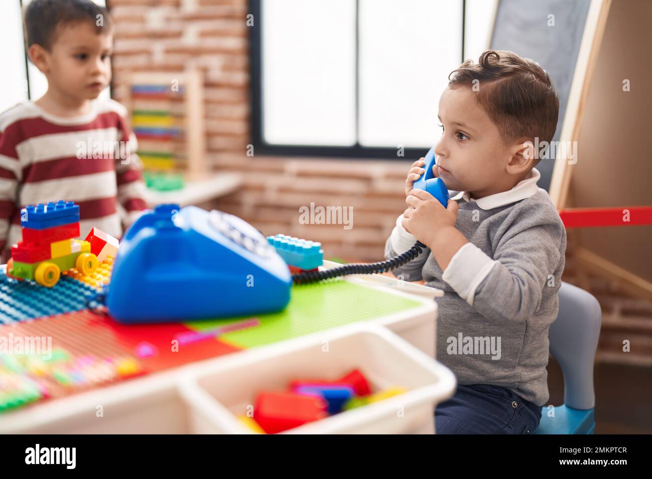 Two kids playing with telephone toy sitting on table at kindergarten ...