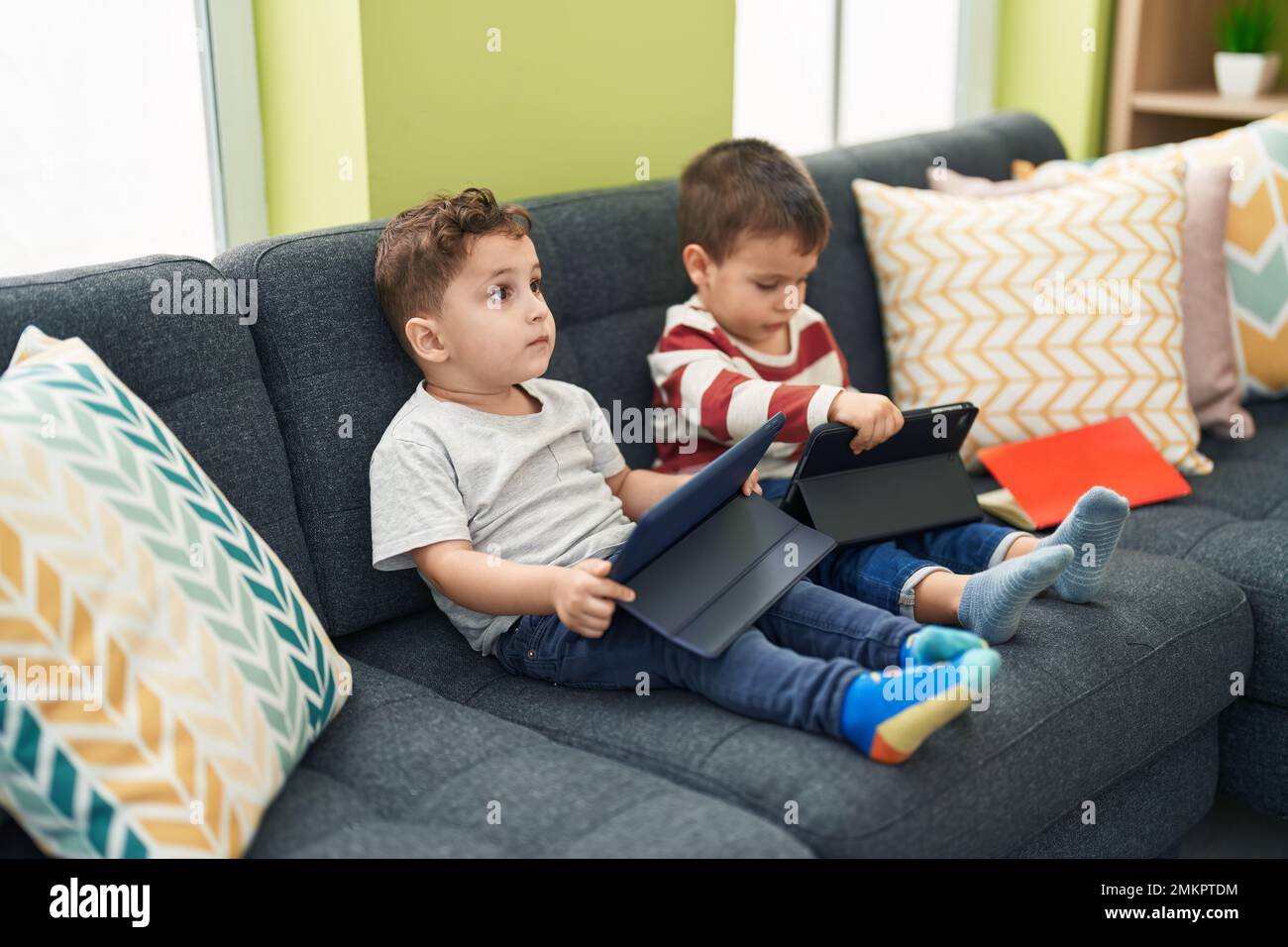 Two kids watching video on touchpad sitting on sofa at home Stock Photo ...