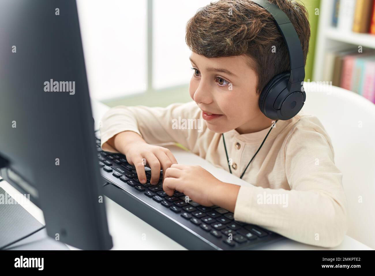 Adorable hispanic boy student using computer sitting on table at ...