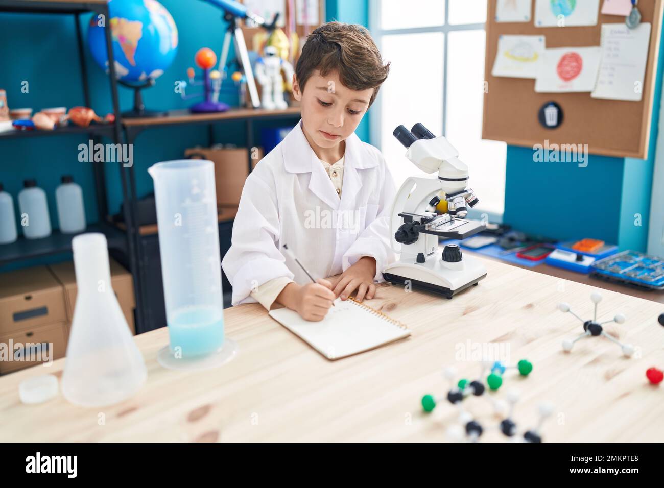 Adorable hispanic boy student using microscope writing on notebook at ...