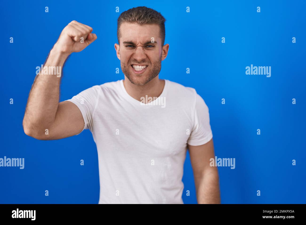 Young caucasian man standing over blue background angry and mad raising ...
