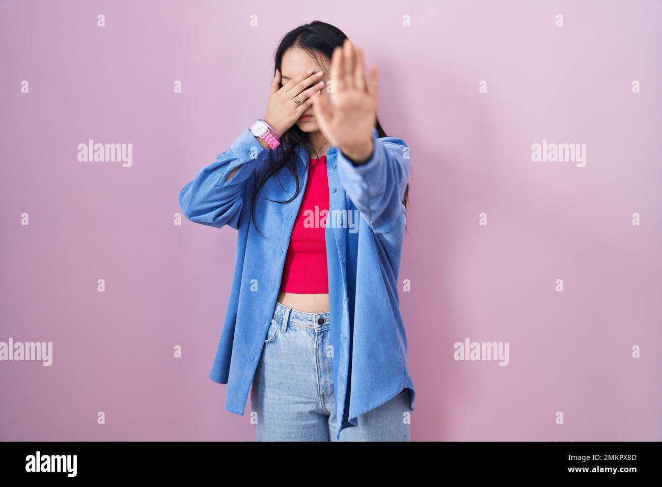 Young asian woman standing over pink background covering eyes with ...