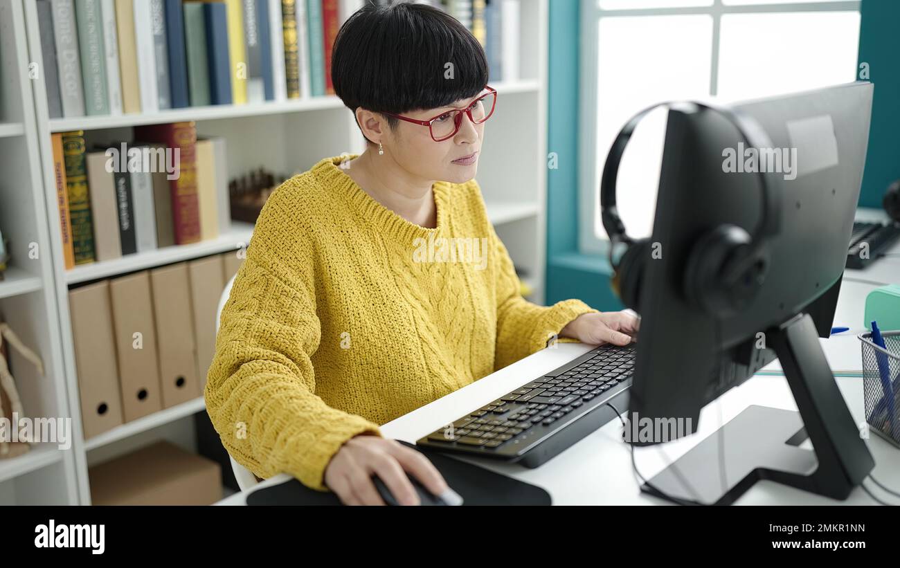 Young chinese woman student using computer studying at library ...