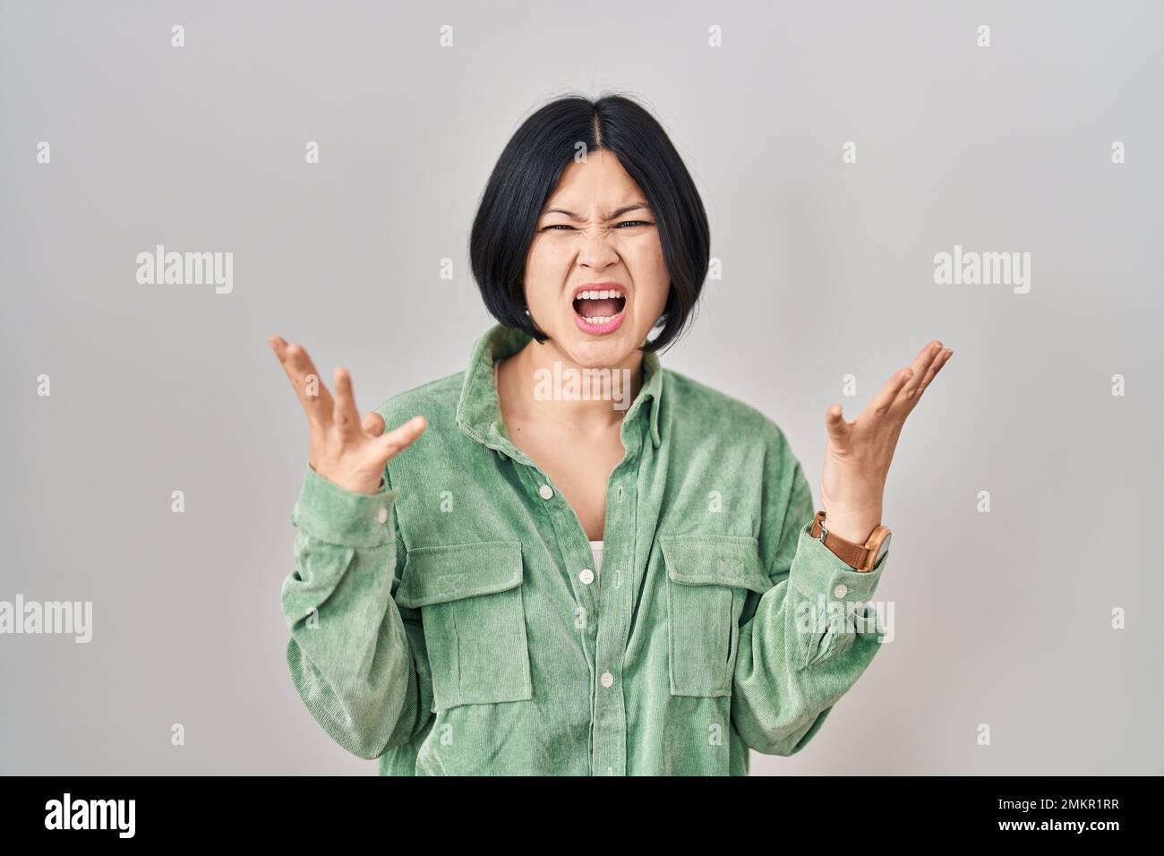 Young asian woman standing over white background crazy and mad shouting ...