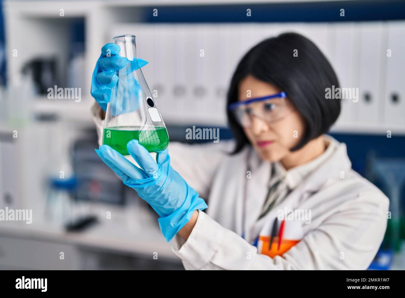 Young chinese woman scientist holding measuring liquid at laboratory ...