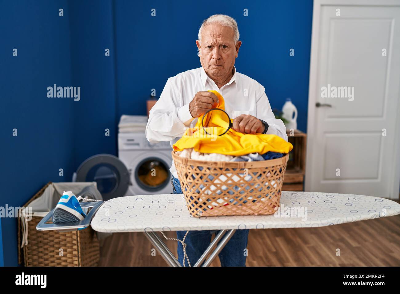 Senior man with grey hair holding magnifying glass looking for stain at ...