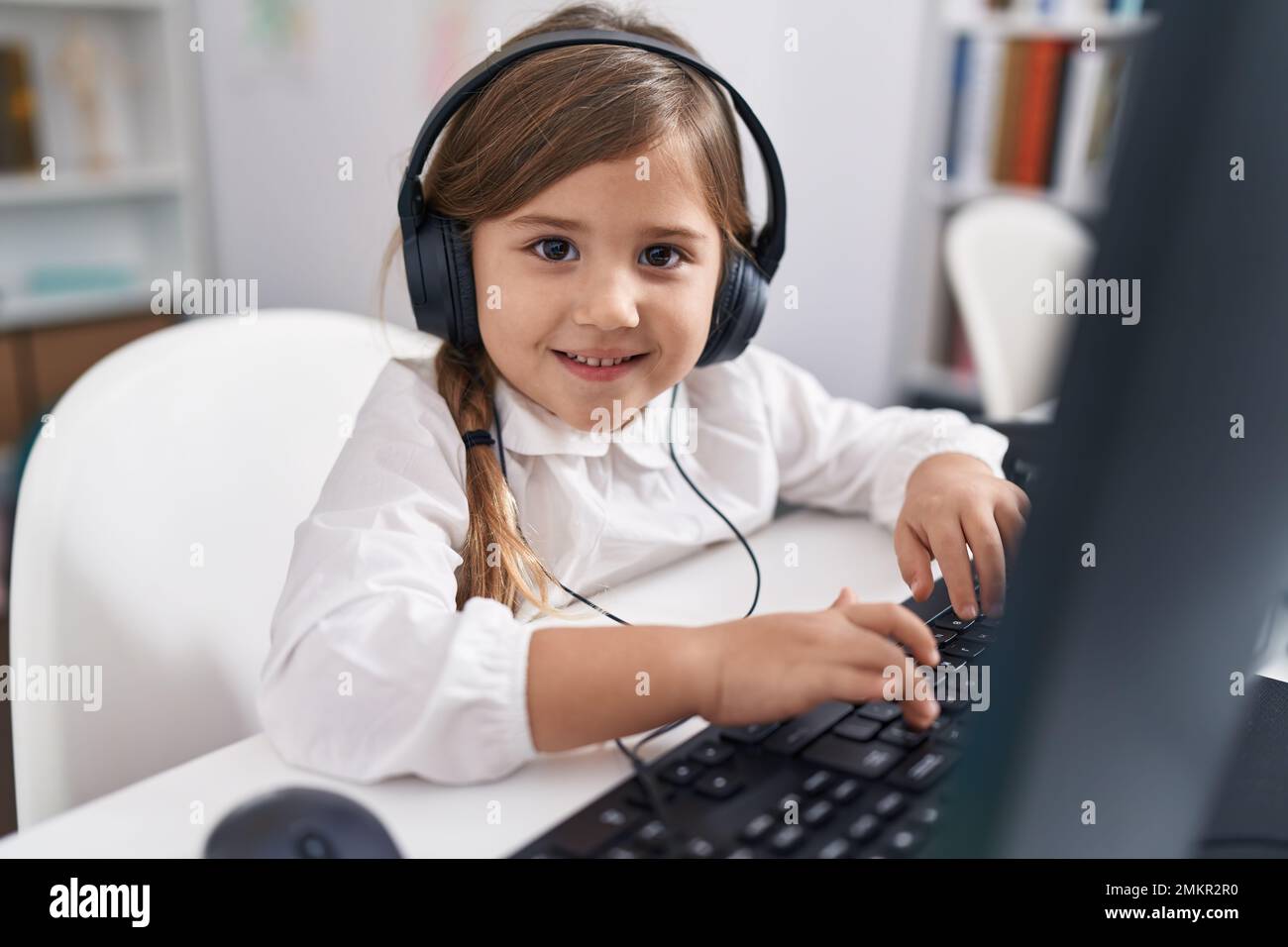 Adorable blonde girl student using computer sitting on table at ...