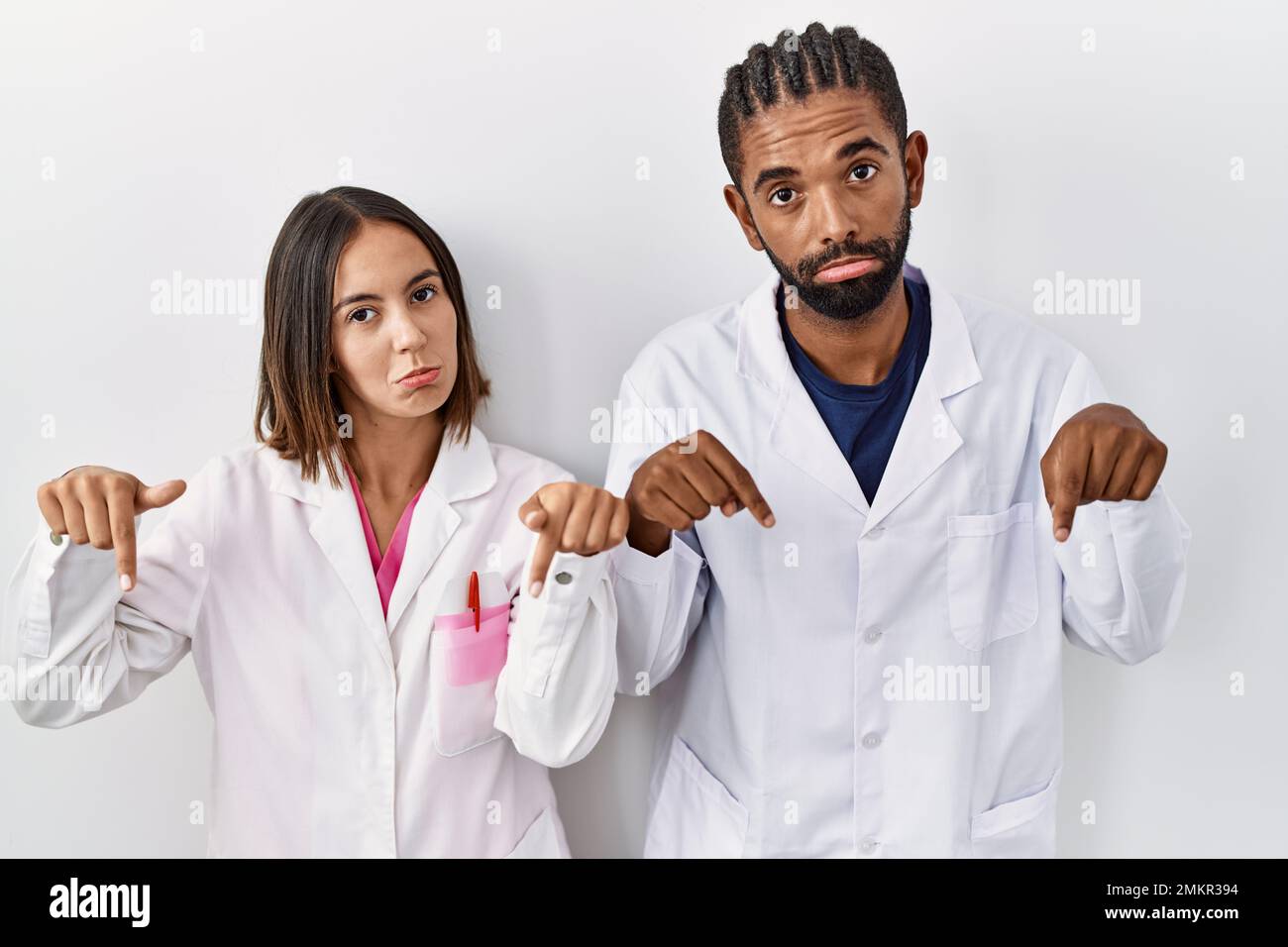 Young hispanic doctors standing over white background pointing down ...