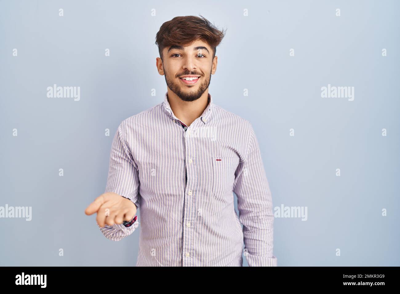 Arab man with beard standing over blue background smiling cheerful ...