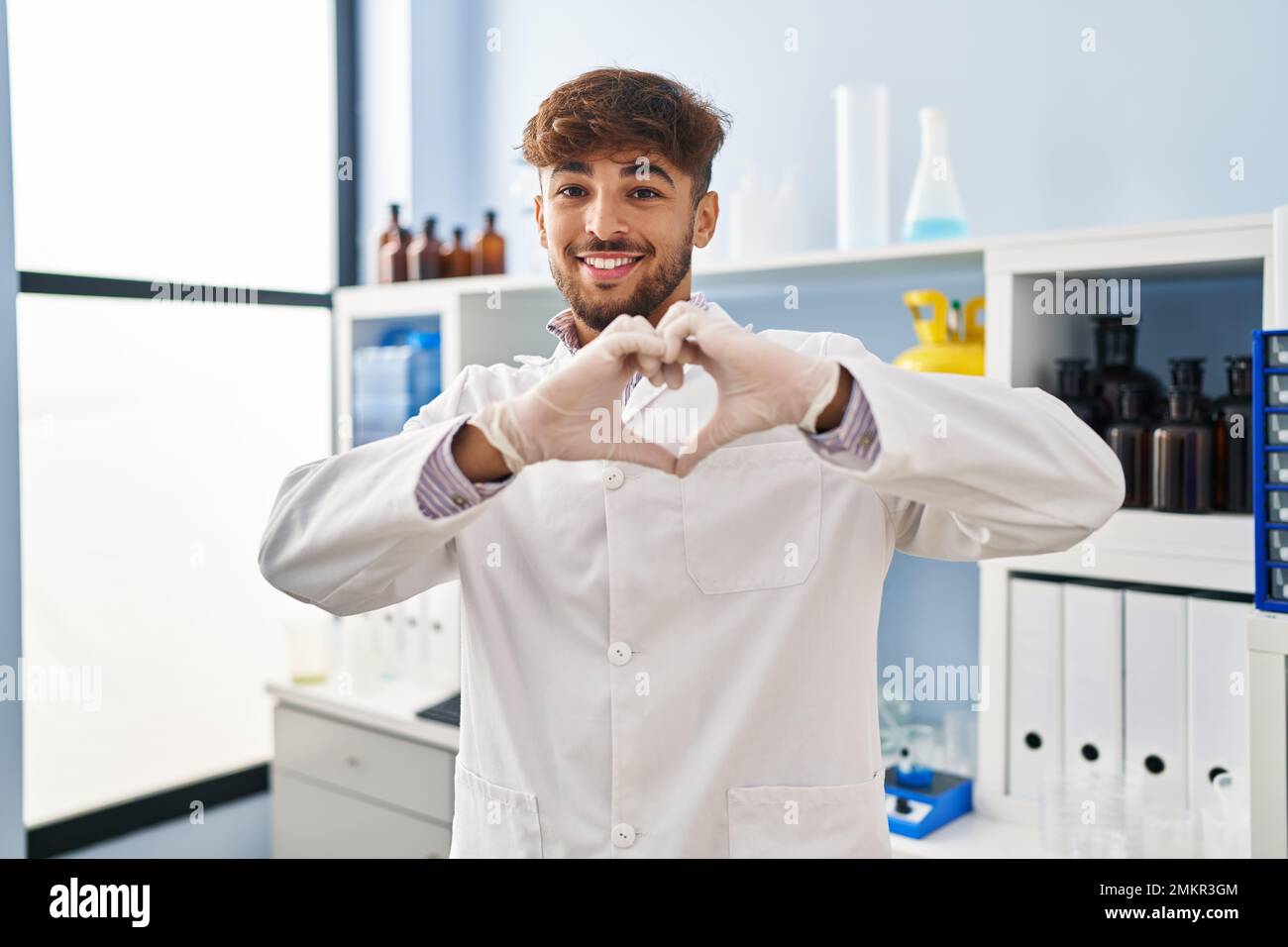 Arab man with beard working at scientist laboratory smiling in love doing heart symbol shape ...