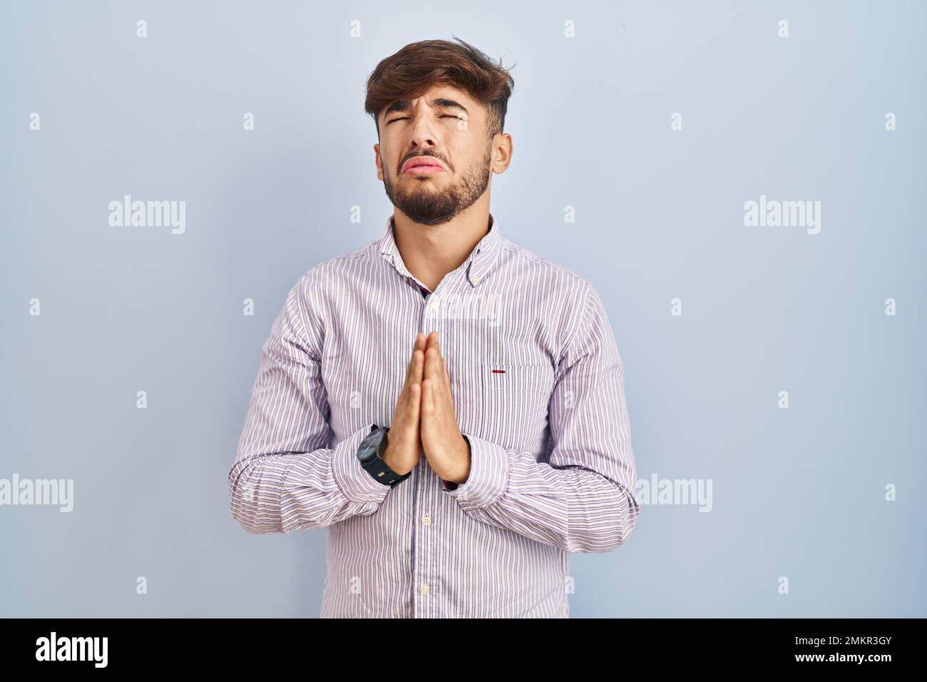 Arab man with beard standing over blue background begging and praying ...