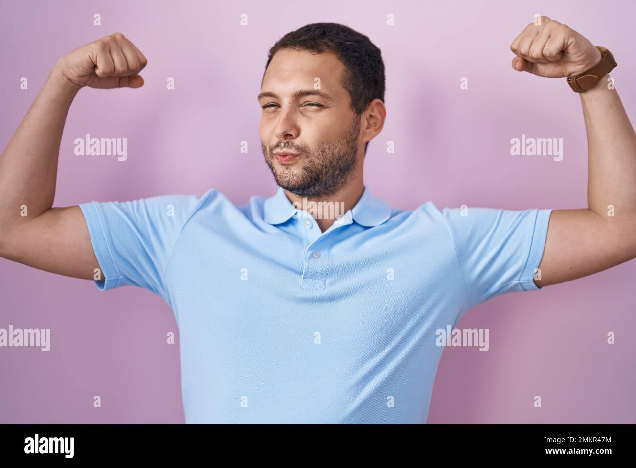 Hispanic man standing over pink background showing arms muscles smiling ...