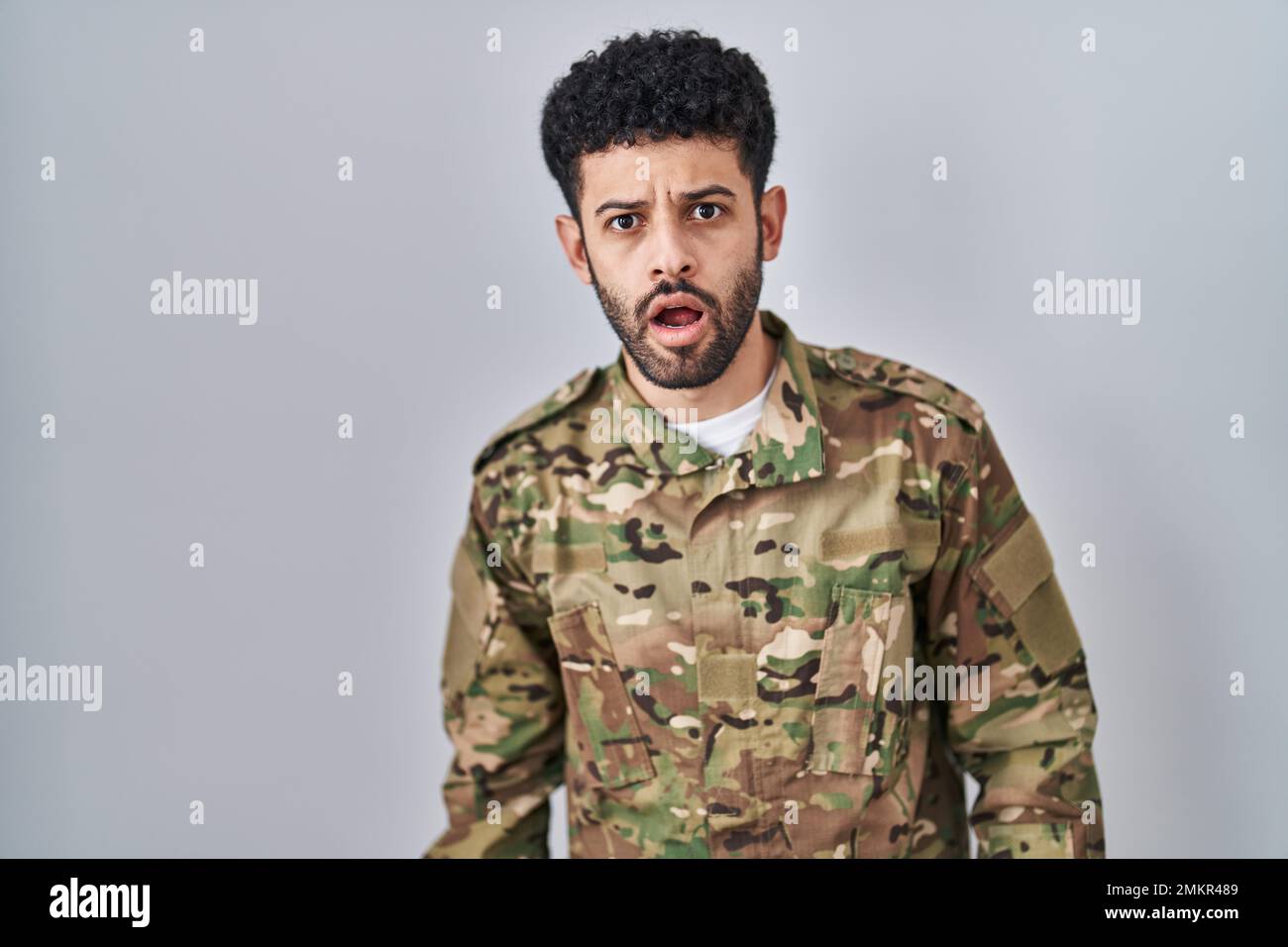 Arab man wearing camouflage army uniform in shock face, looking ...